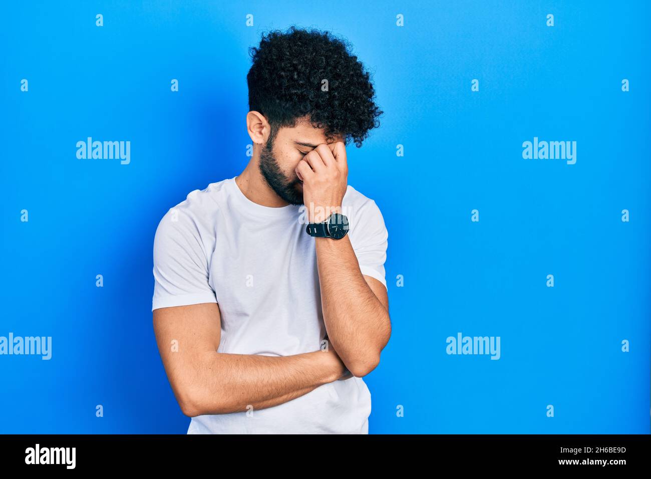Young arab man with beard wearing casual white t shirt tired rubbing ...