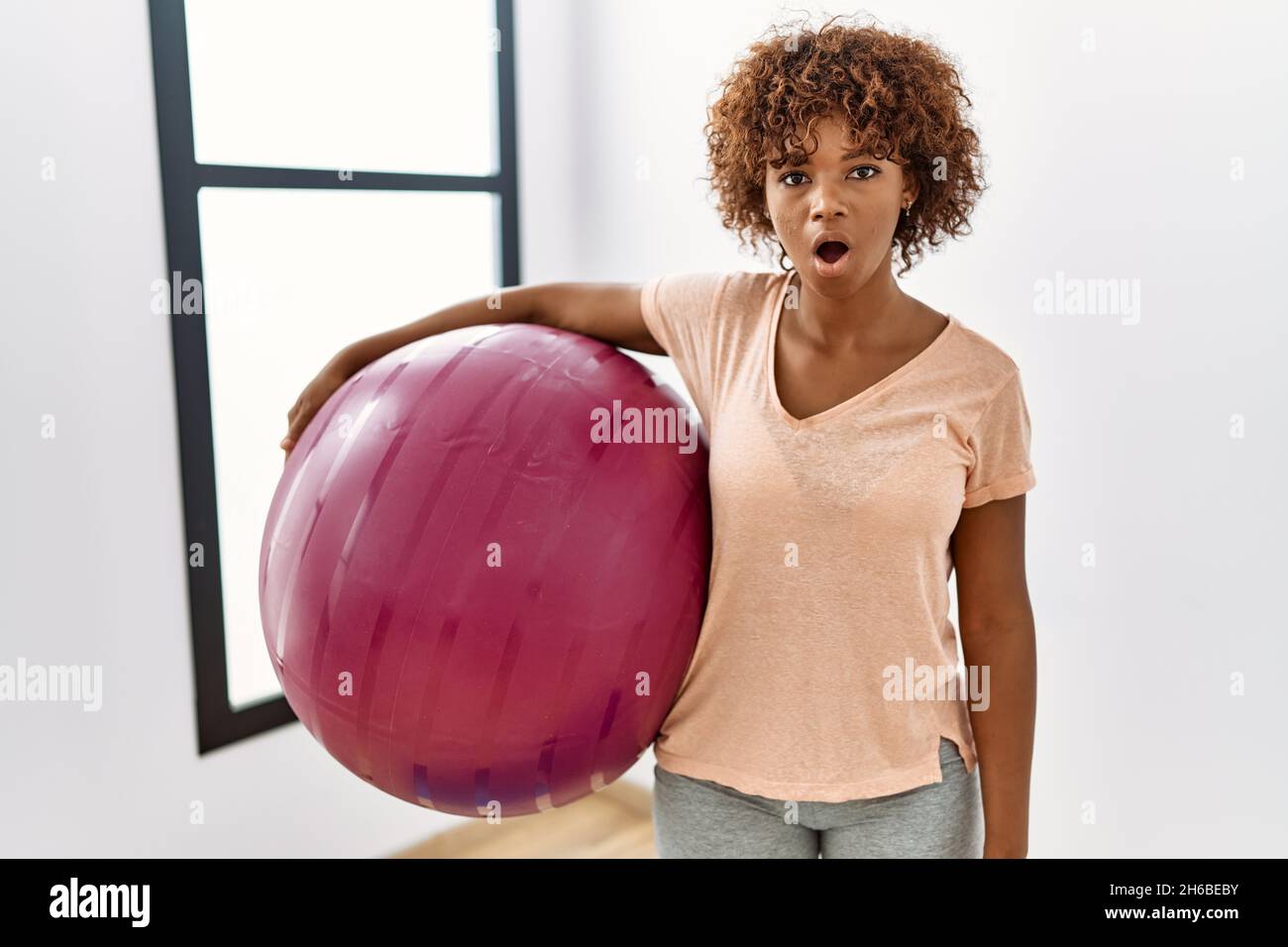 Young african american woman holding pilates ball scared and amazed ...