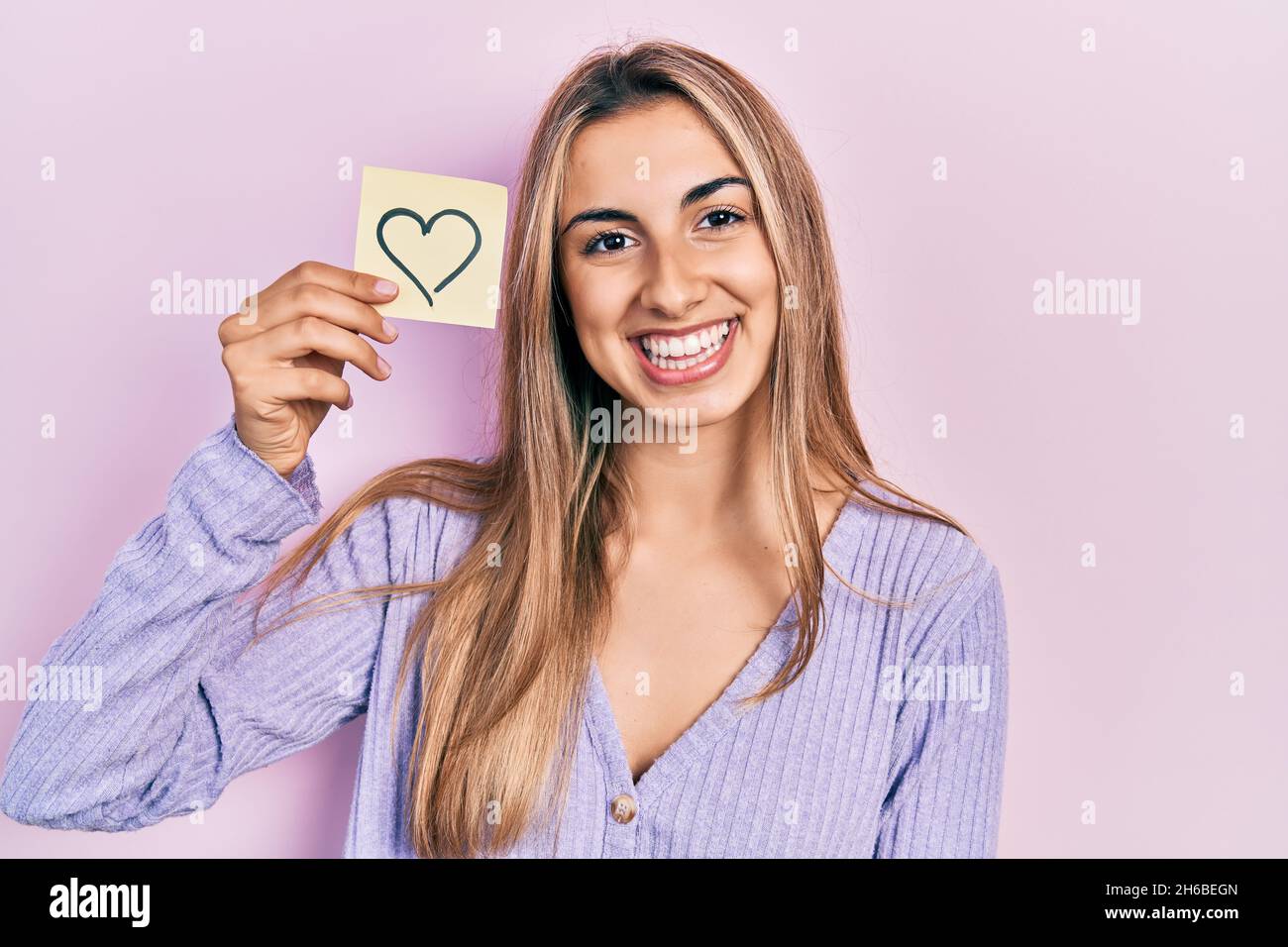 Beautiful hispanic woman holding heart reminder looking positive and ...