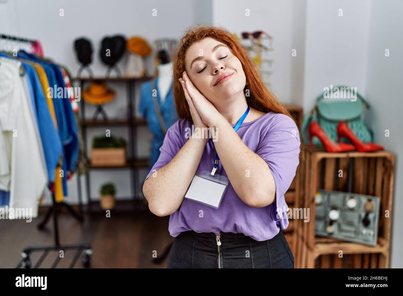 Young redhead woman working as manager at retail boutique sleeping tired dreaming and posing ...