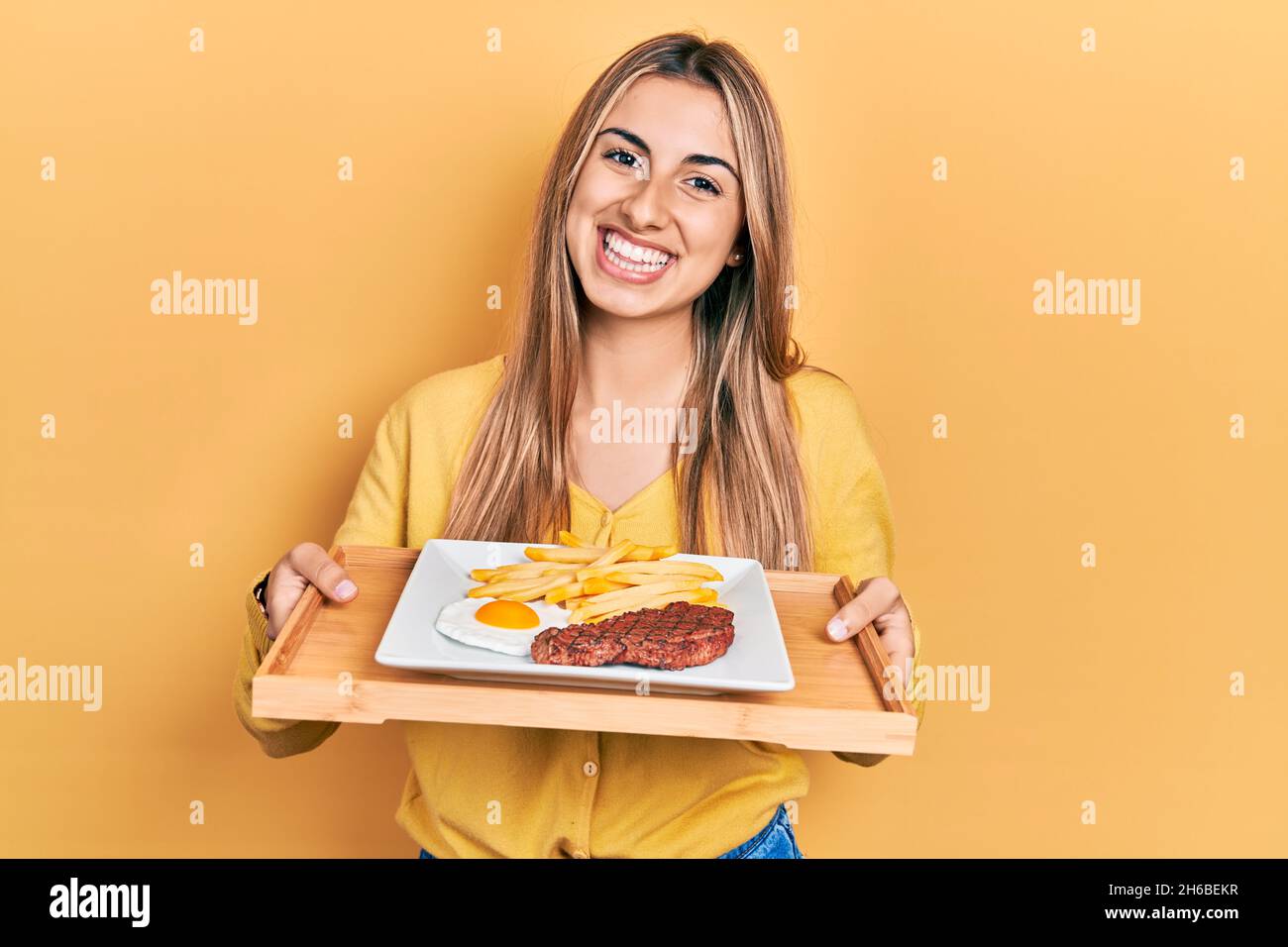 Beautiful hispanic woman holding tray with meat loaf and fried egg ...