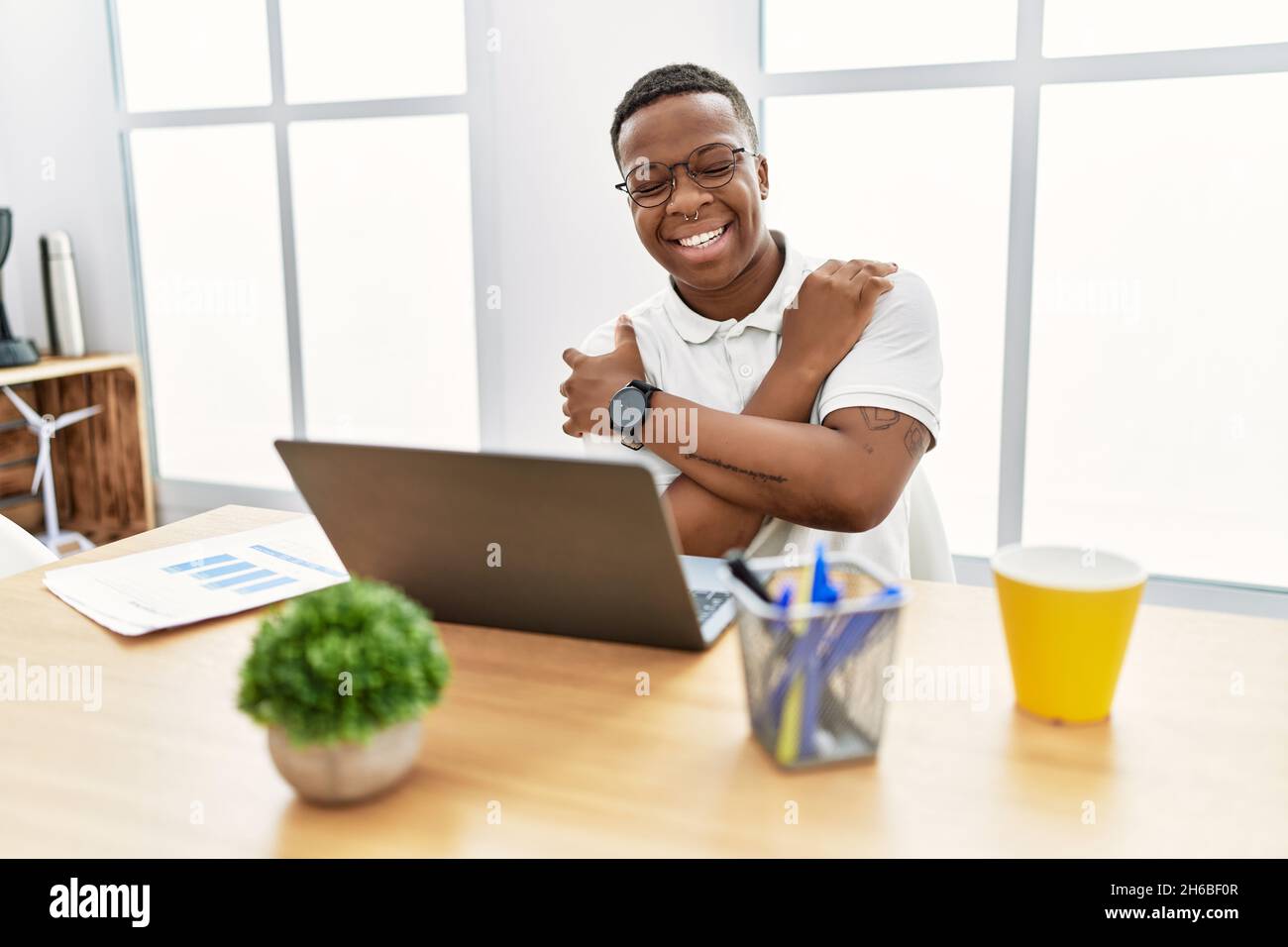 Young african man working at the office using computer laptop hugging ...