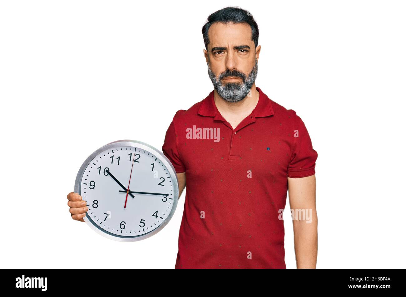 Middle aged man with beard holding big clock thinking attitude and ...