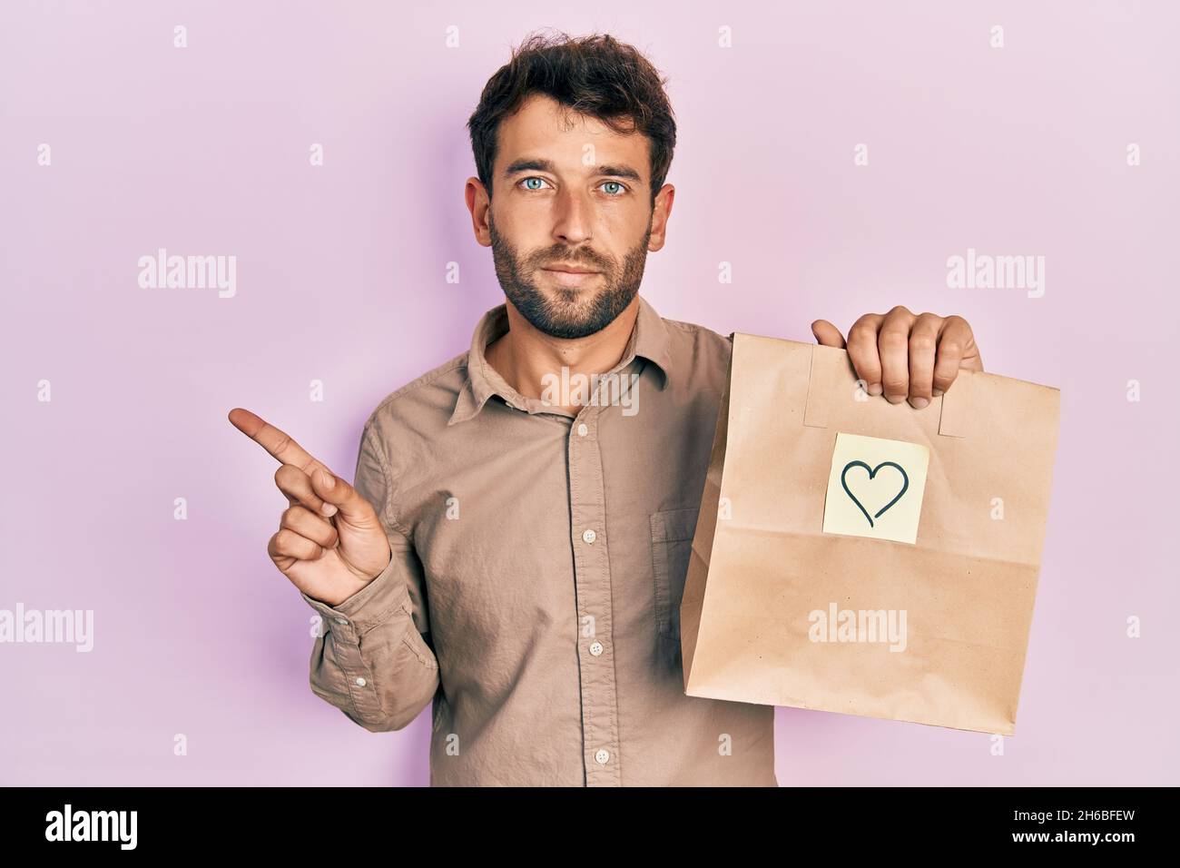 Handsome man with beard holding delivery paper bag with heart reminder ...
