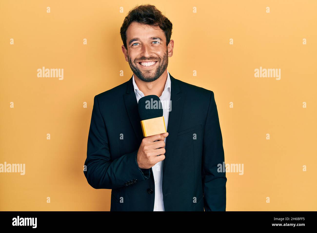 Handsome man with beard holding reporter microphone looking positive ...