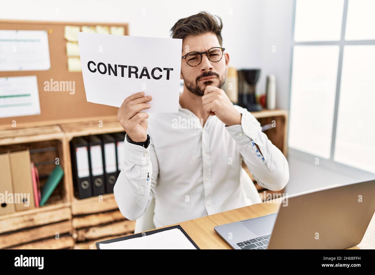 Young man with beard holding contract paper at the office serious face ...