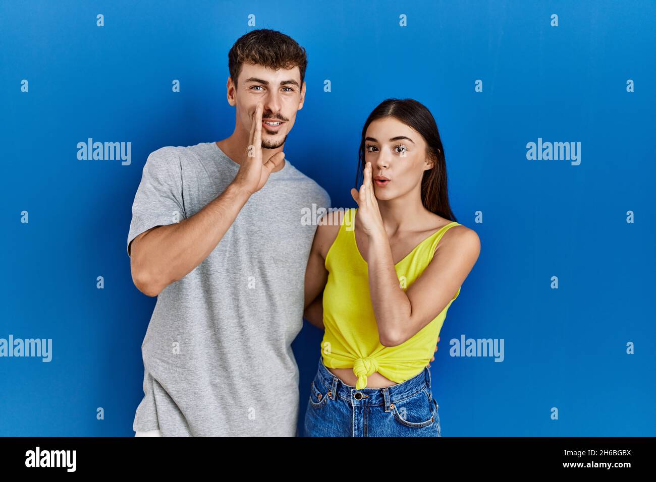 Young hispanic couple standing together over blue background hand on ...