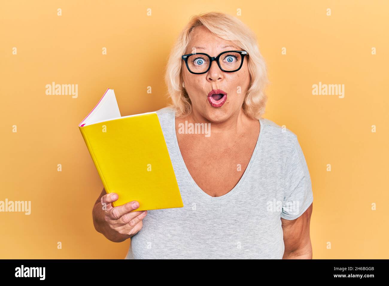 Middle age blonde woman reading a book scared and amazed with open ...