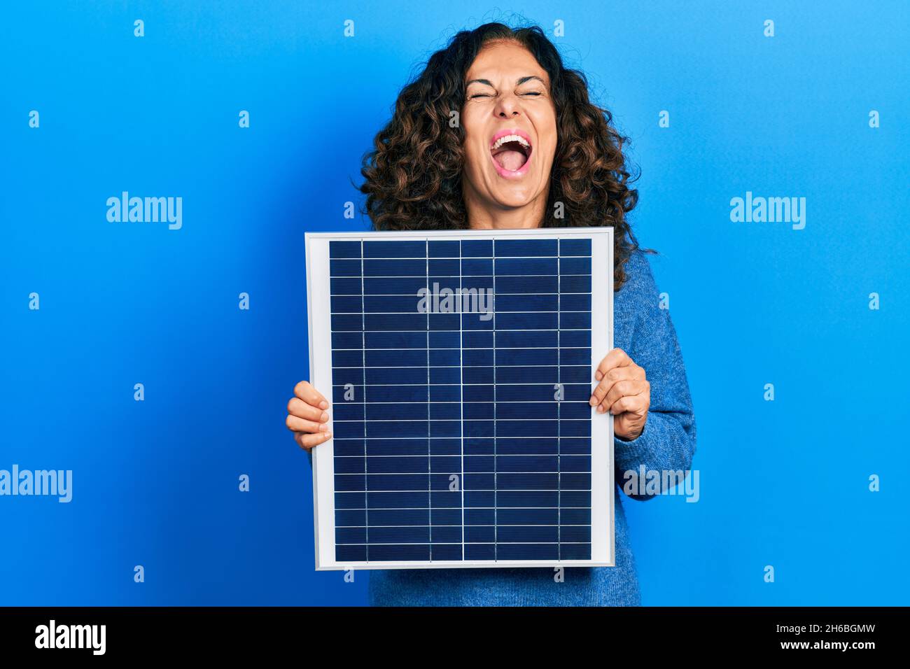 Middle age hispanic woman holding photovoltaic solar panel angry and ...