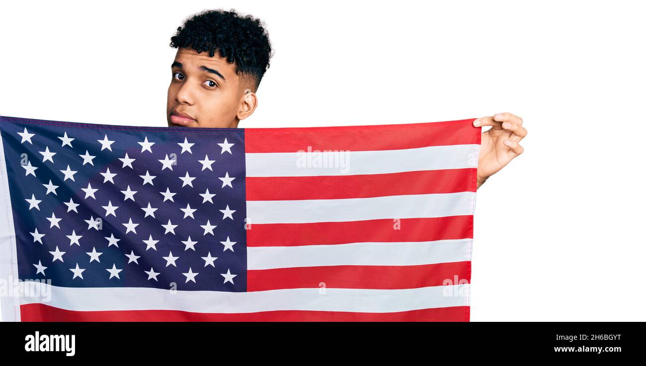Young african american man holding united states flag clueless and ...