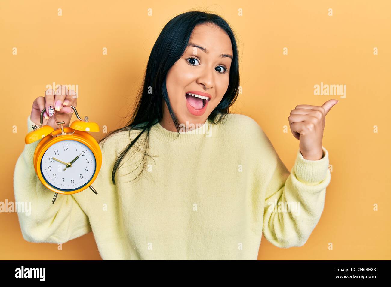 Beautiful hispanic woman with nose piercing holding alarm clock ...