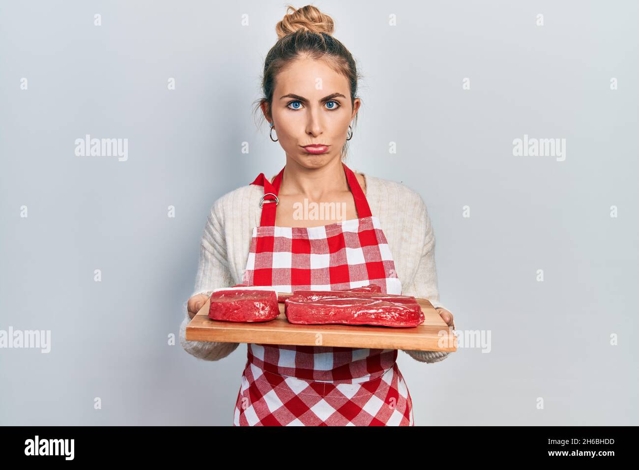 Young caucasian woman holding board with raw meat depressed and worry ...