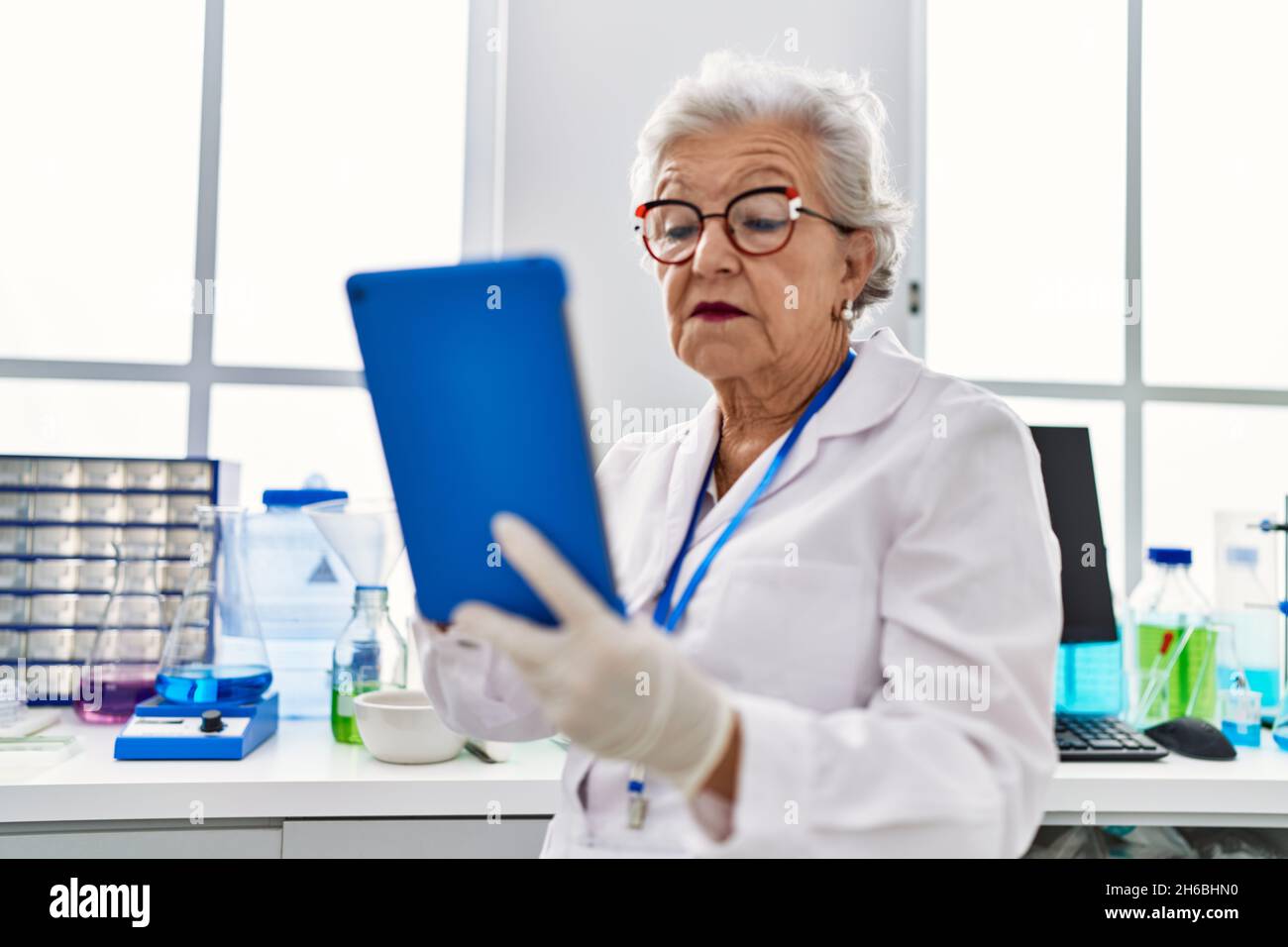 Senior grey-haired woman wearing scientist uniform using touchpad at laboratory Stock Photo - Alamy