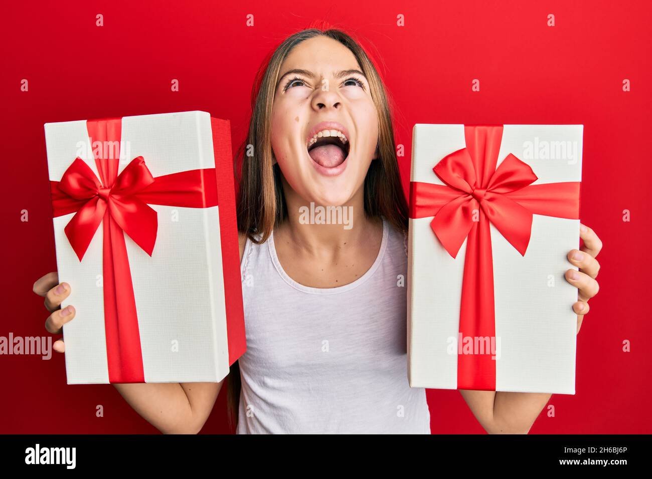 Beautiful brunette little girl holding gifts angry and mad screaming ...