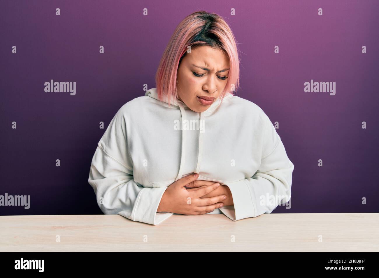 Hispanic woman with pink hair wearing casual sweatshirt sitting on the ...