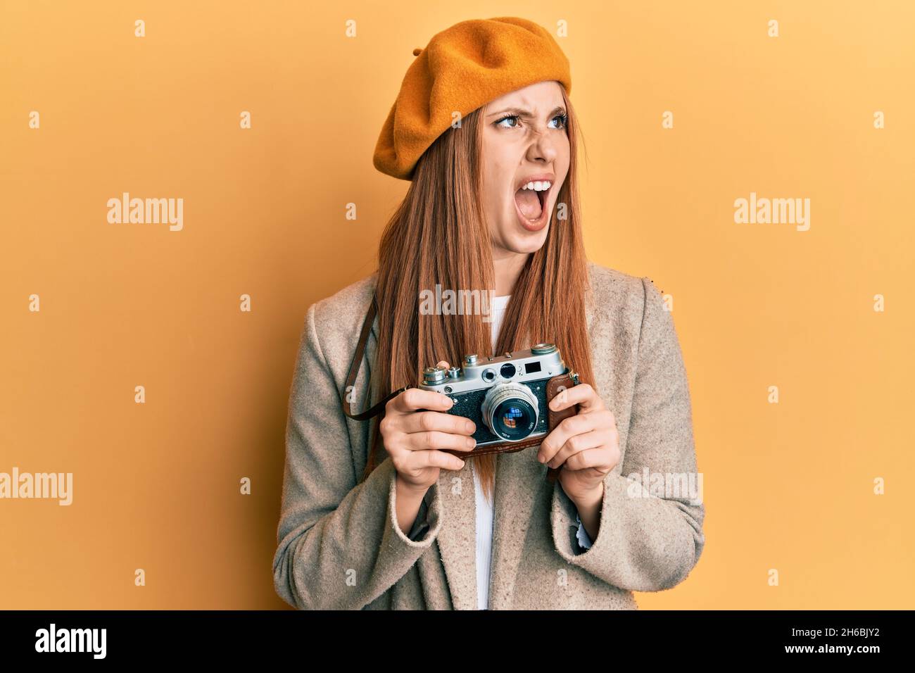 Young irish woman holding vintage camera angry and mad screaming ...