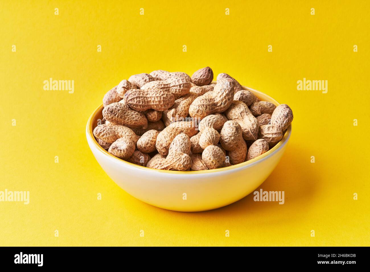 Bowl of peanuts with shell on a yellow background Stock Photo - Alamy