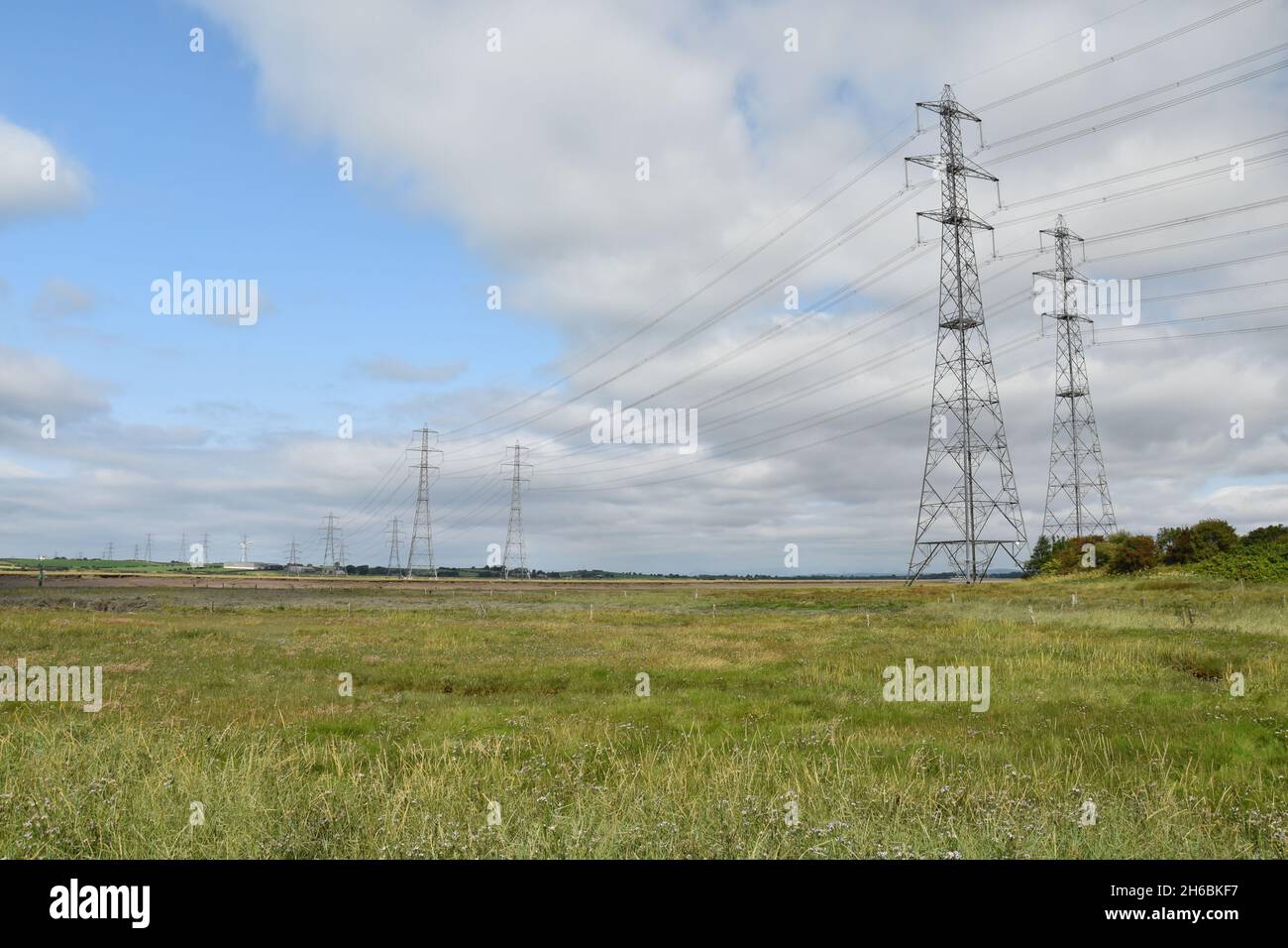 The electricity pylons in the countryside on a green field and blue sky ...