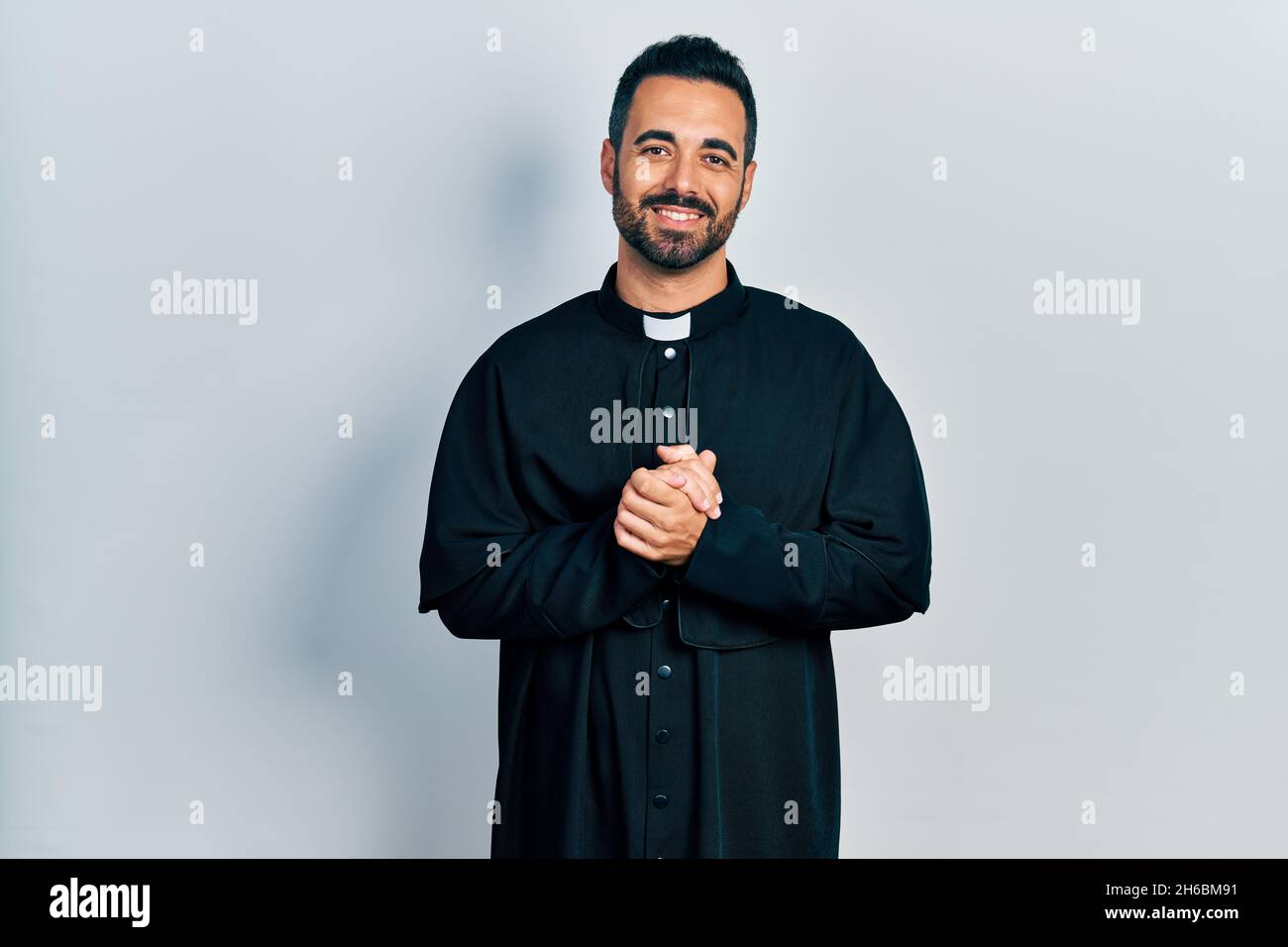 Handsome hispanic man with beard wearing catholic priest robe with ...