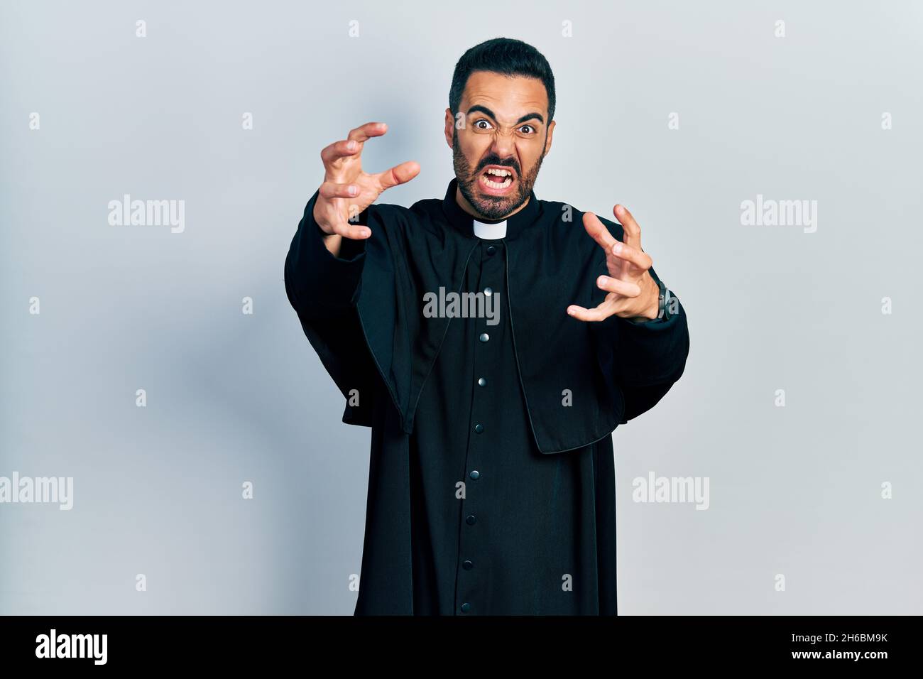 Handsome hispanic man with beard wearing catholic priest robe shouting ...