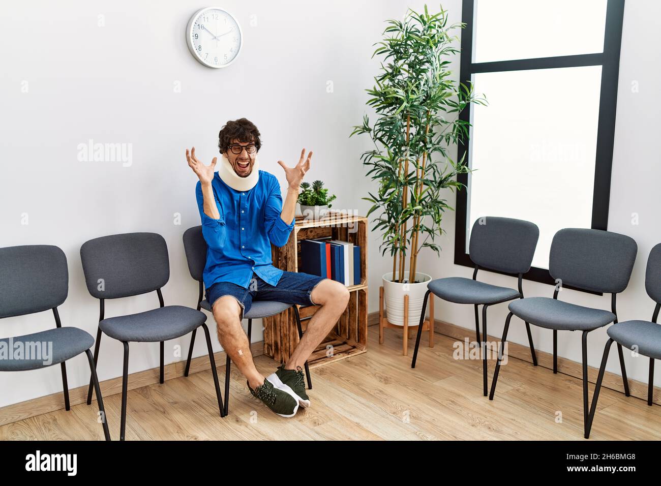 Young hispanic man sitting at doctor waiting room with neck injury ...