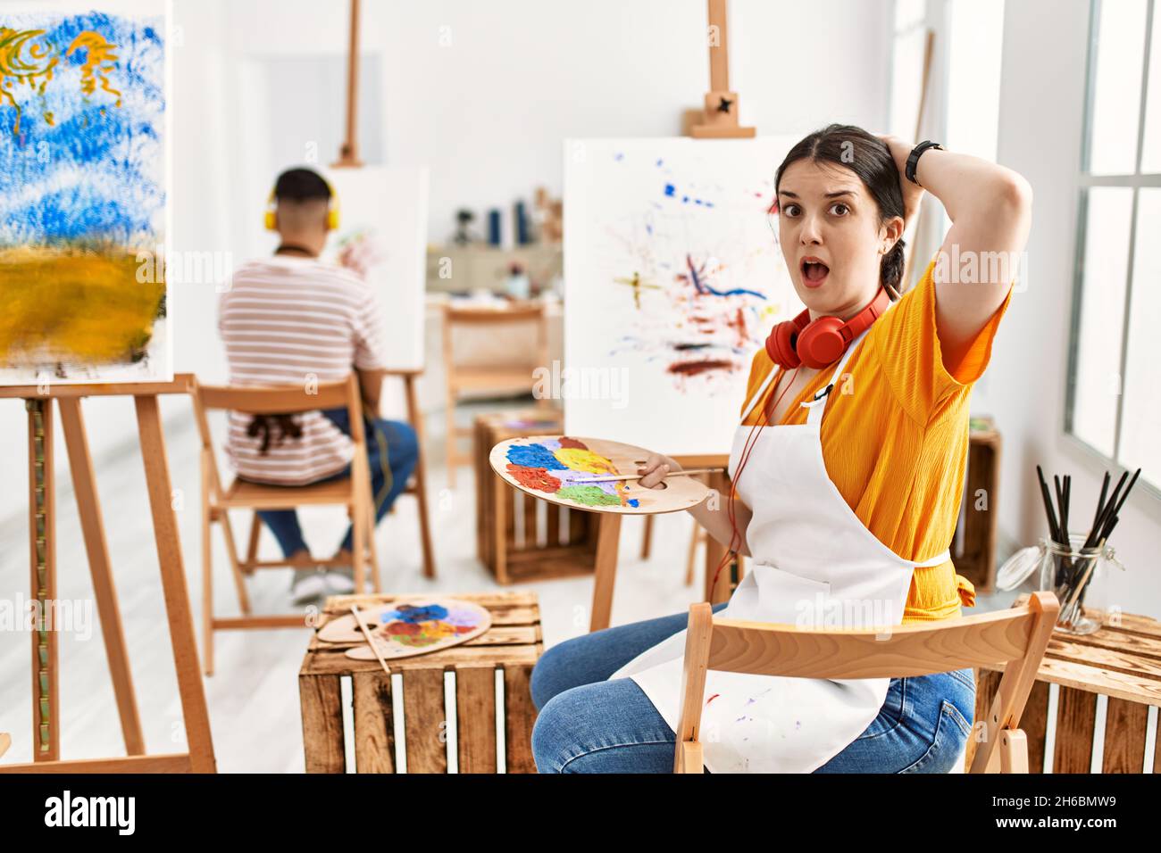 Young artist woman painting on canvas at art studio crazy and scared ...
