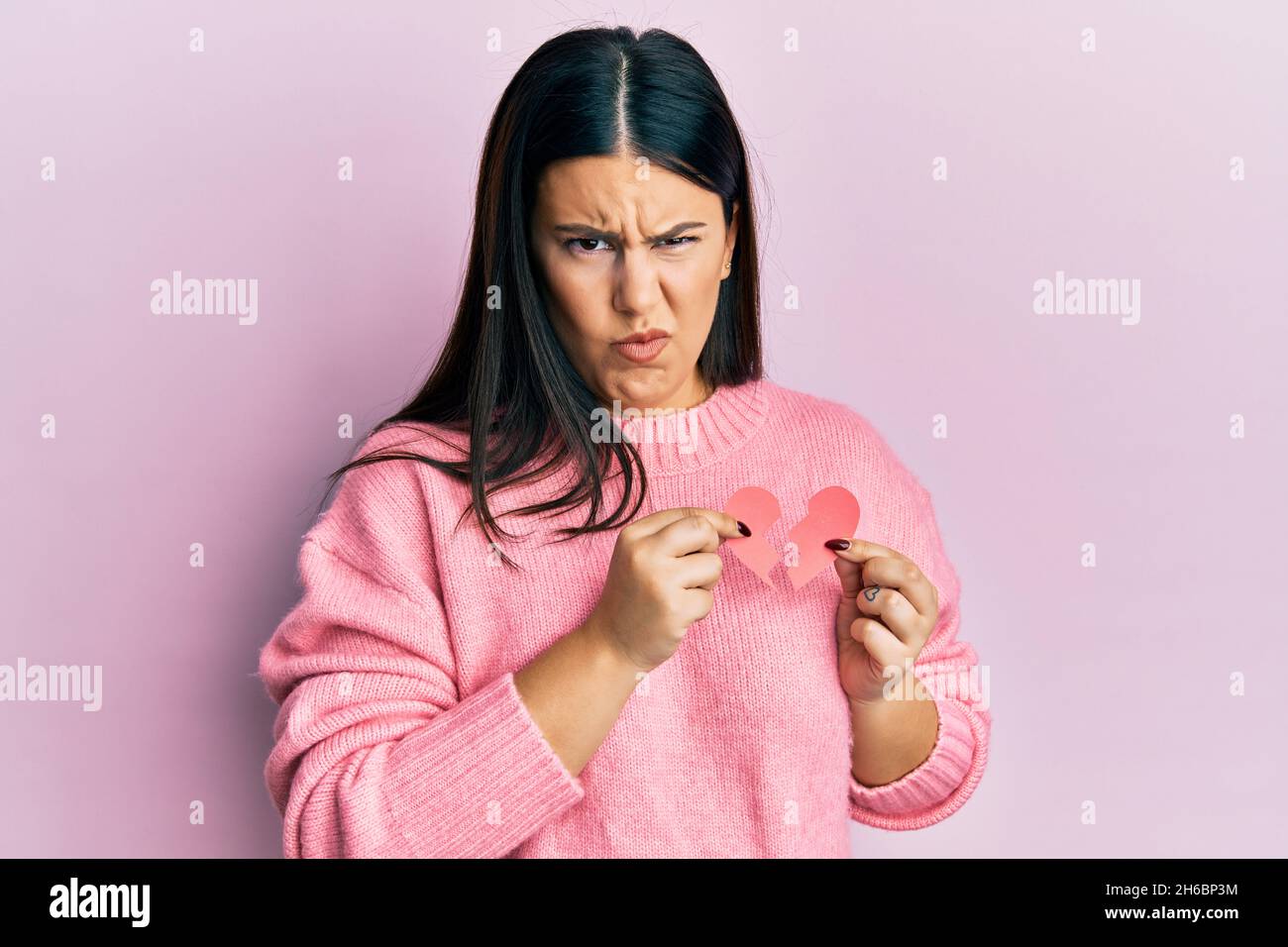 Beautiful brunette woman holding broken heart paper shape skeptic and ...