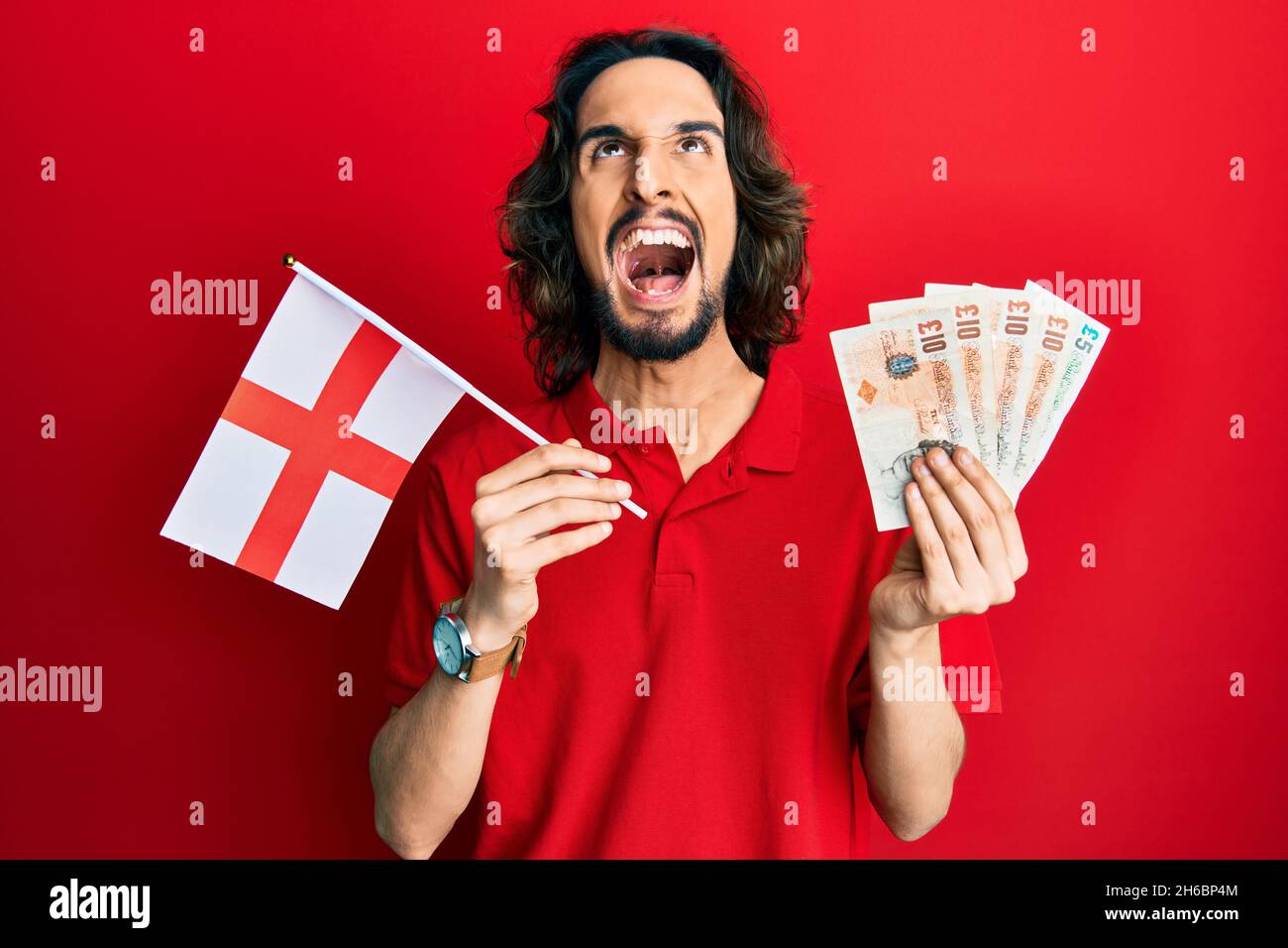 Young hispanic man holding england flag and pounds banknotes angry and ...