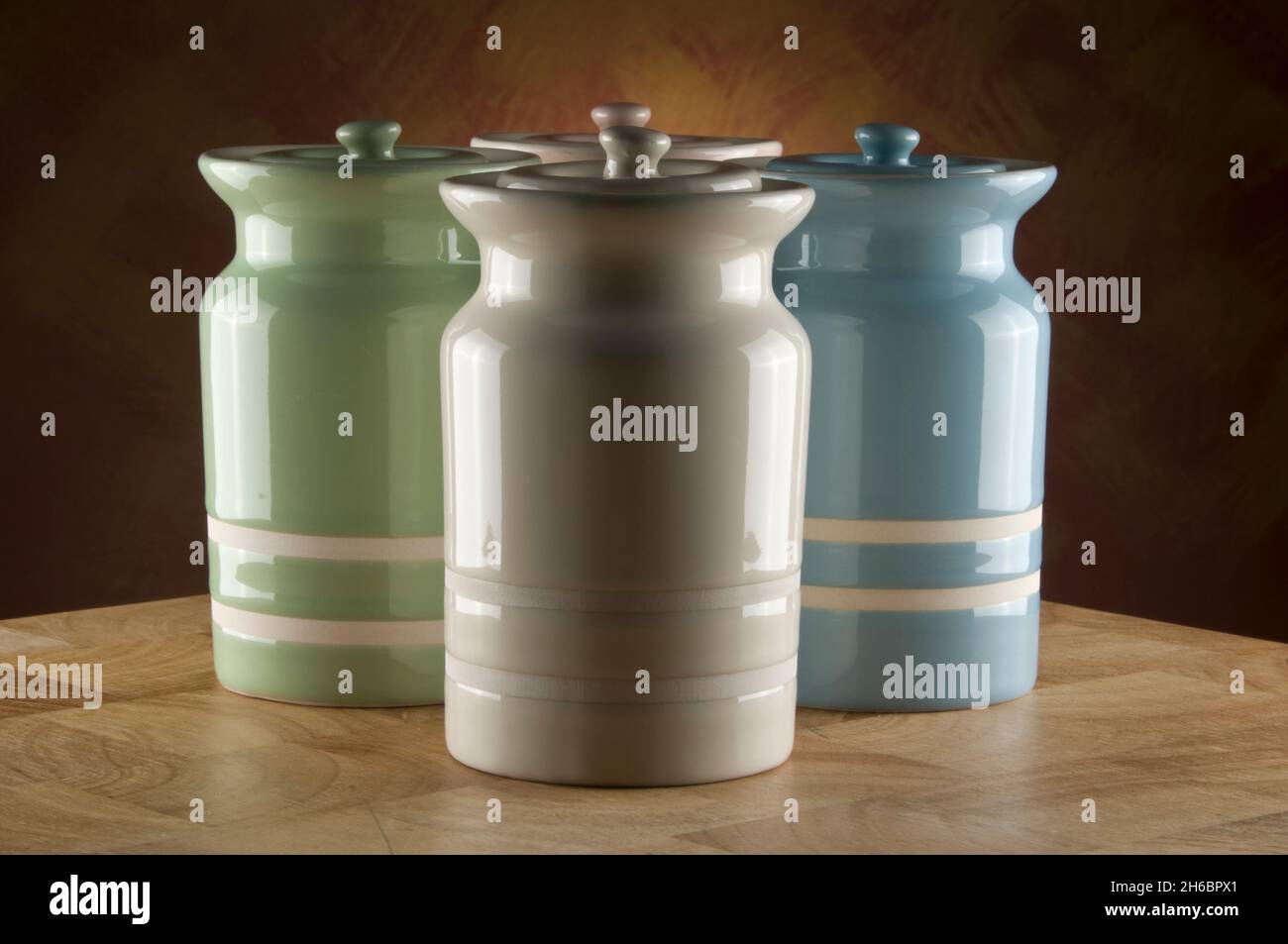 Four colourful ceramic canisters on timber bench with rustic background ...
