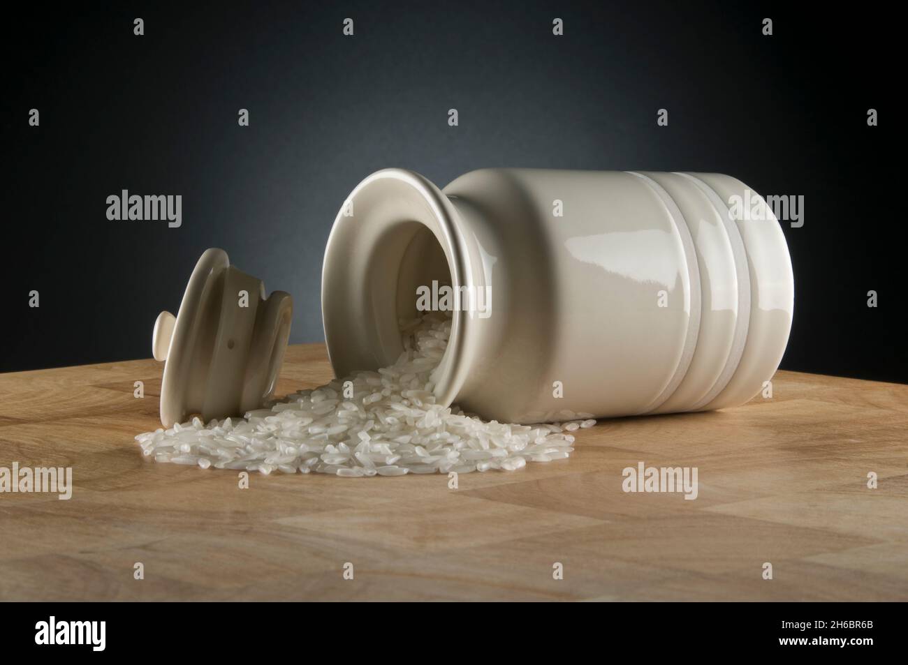 Ceramic canister lying on its side on wood bench with rice spilling out ...