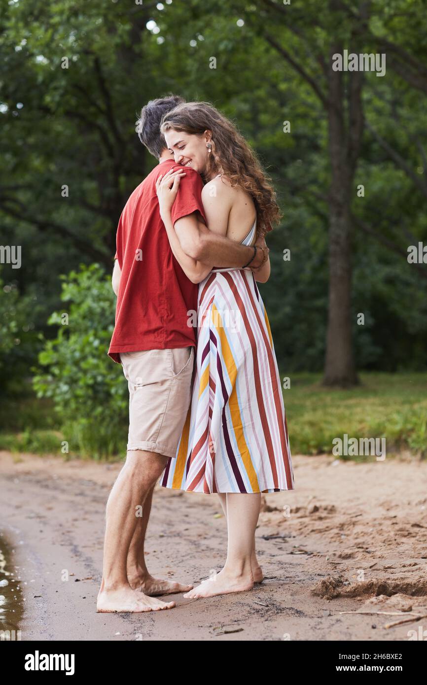 Vertical full length portrait of barefoot young couple embracing while ...