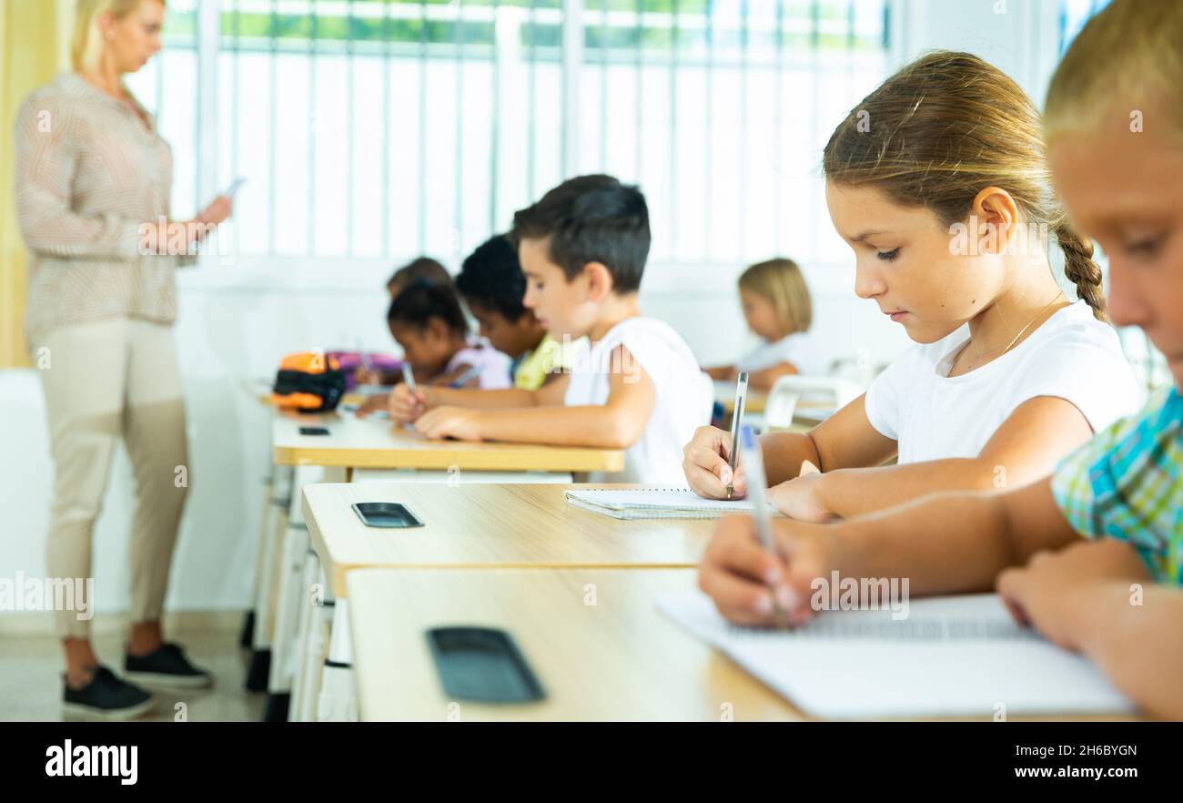 Side view of group of primary school students and positive girl at desk ...
