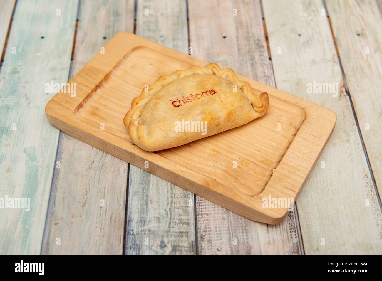 Argentine empanada stuffed with Spanish chistorra stew on wooden plate ...