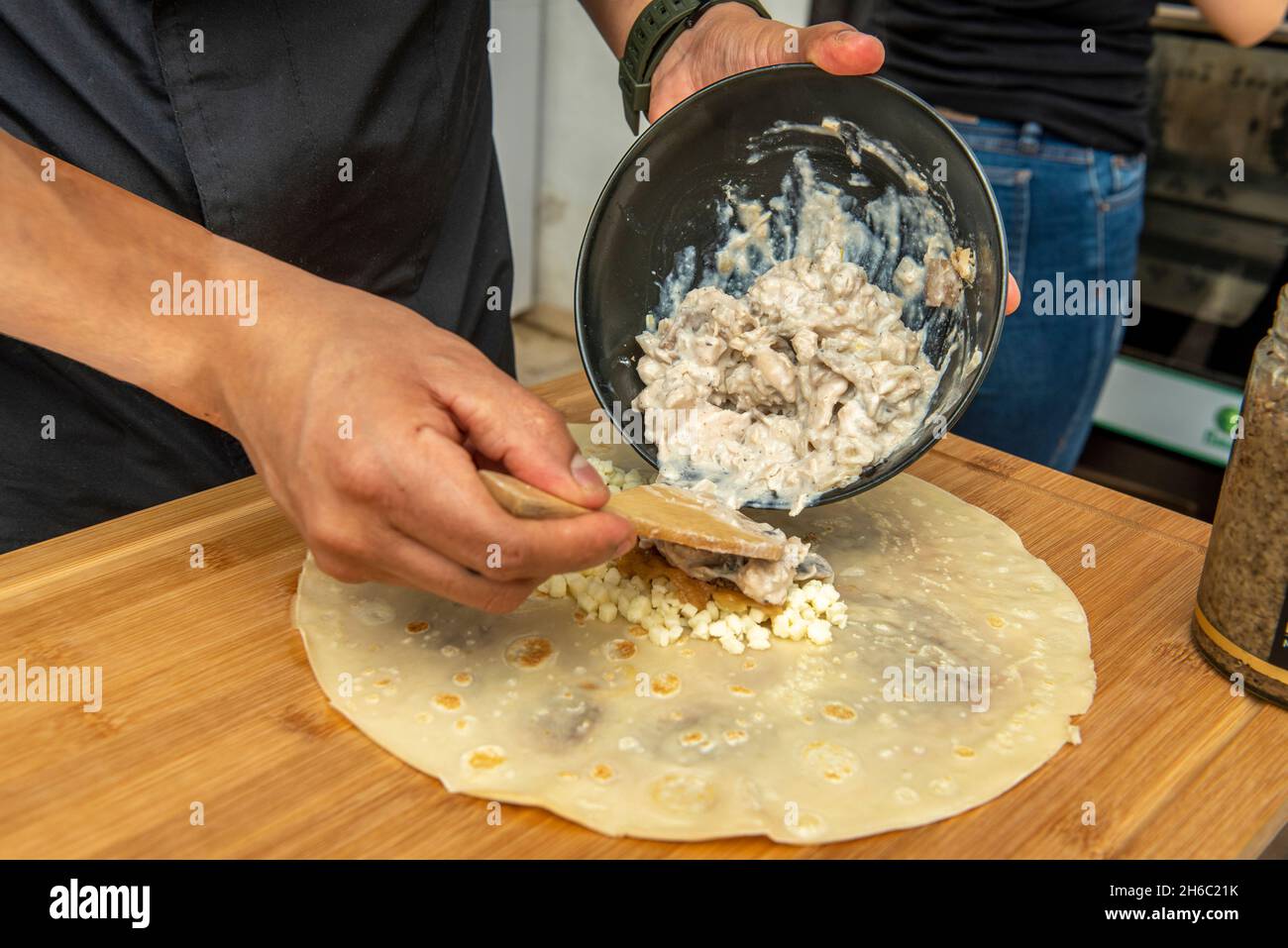 Men hands filling a fresh cheese crepe with stewed mushrooms and melted ...