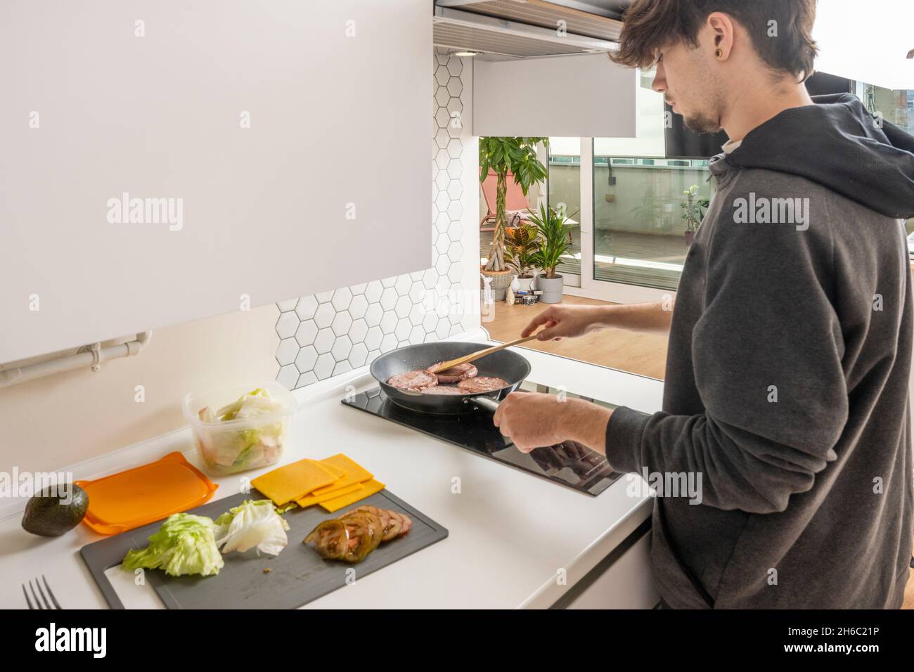 Teenage girl cooking burgers with cheddar cheese, tomato slices and ...