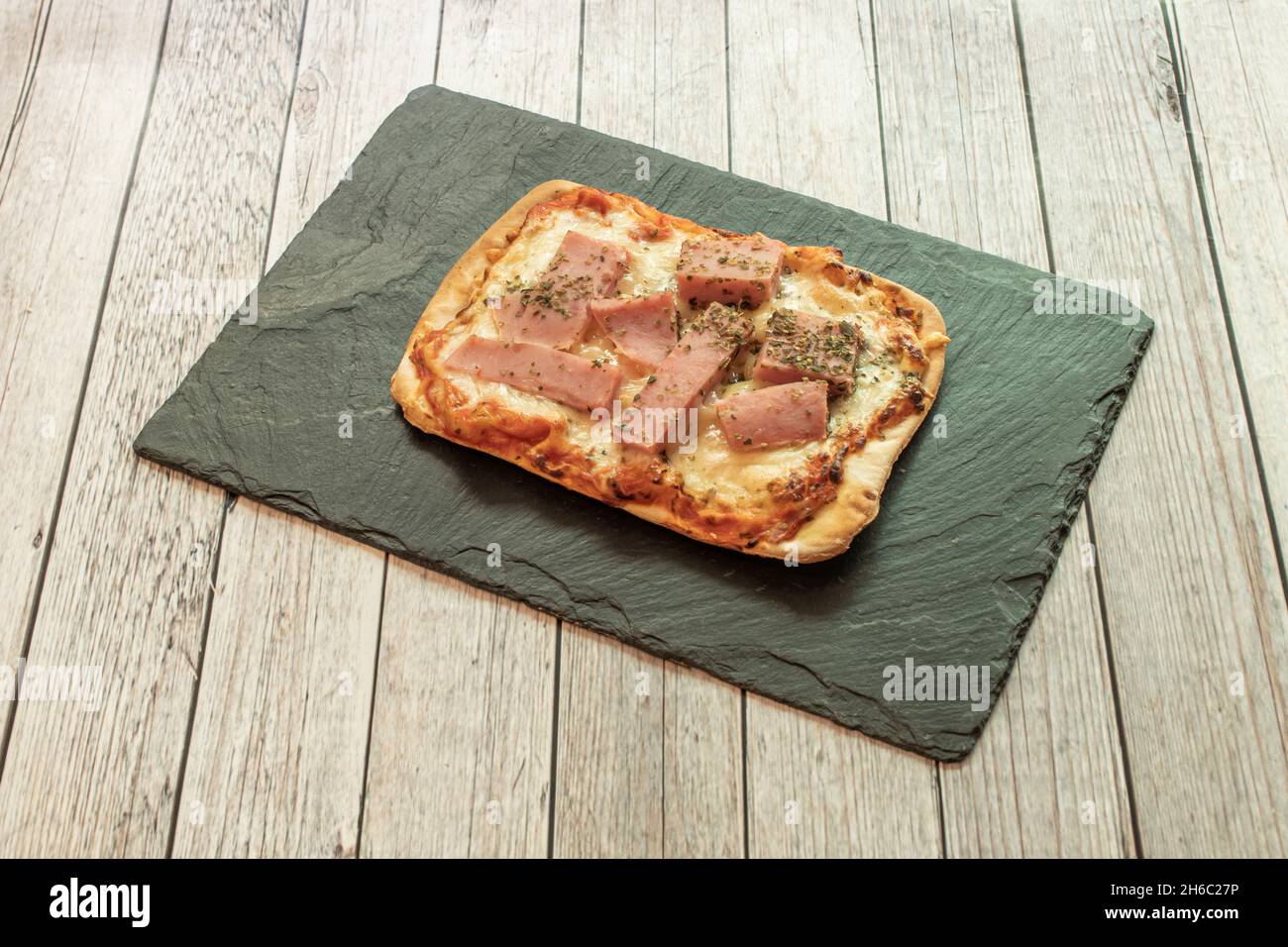 Mini rectangular pizza of cooked ham with mozzarella cheese on black ...