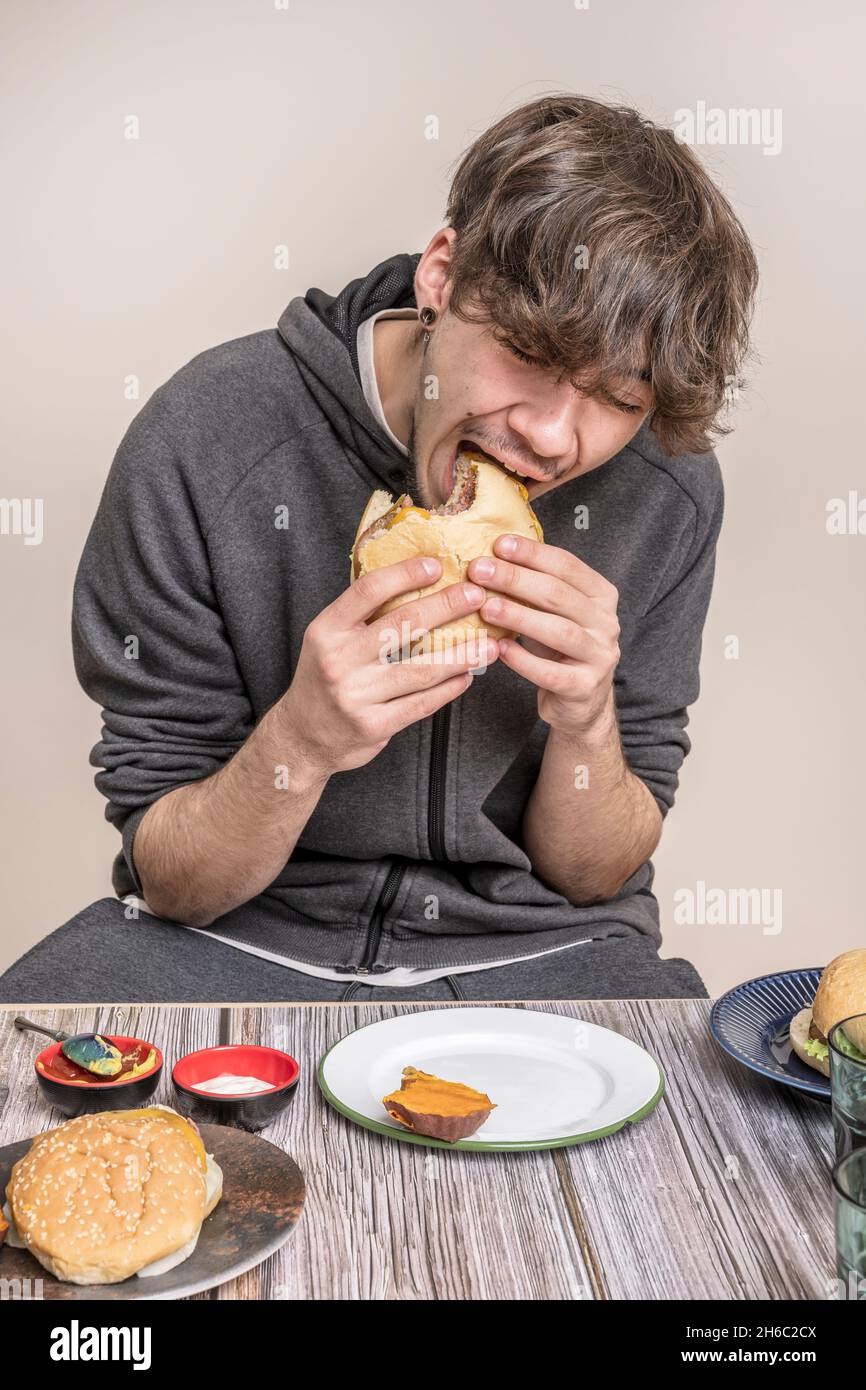 Young man biting into a beef burger with relish Stock Photo - Alamy