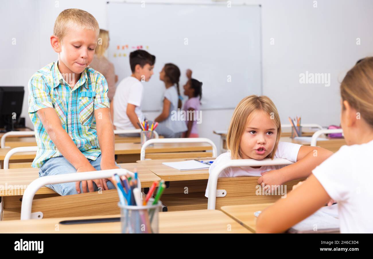 Positive primary school students are talking about homework at desk ...