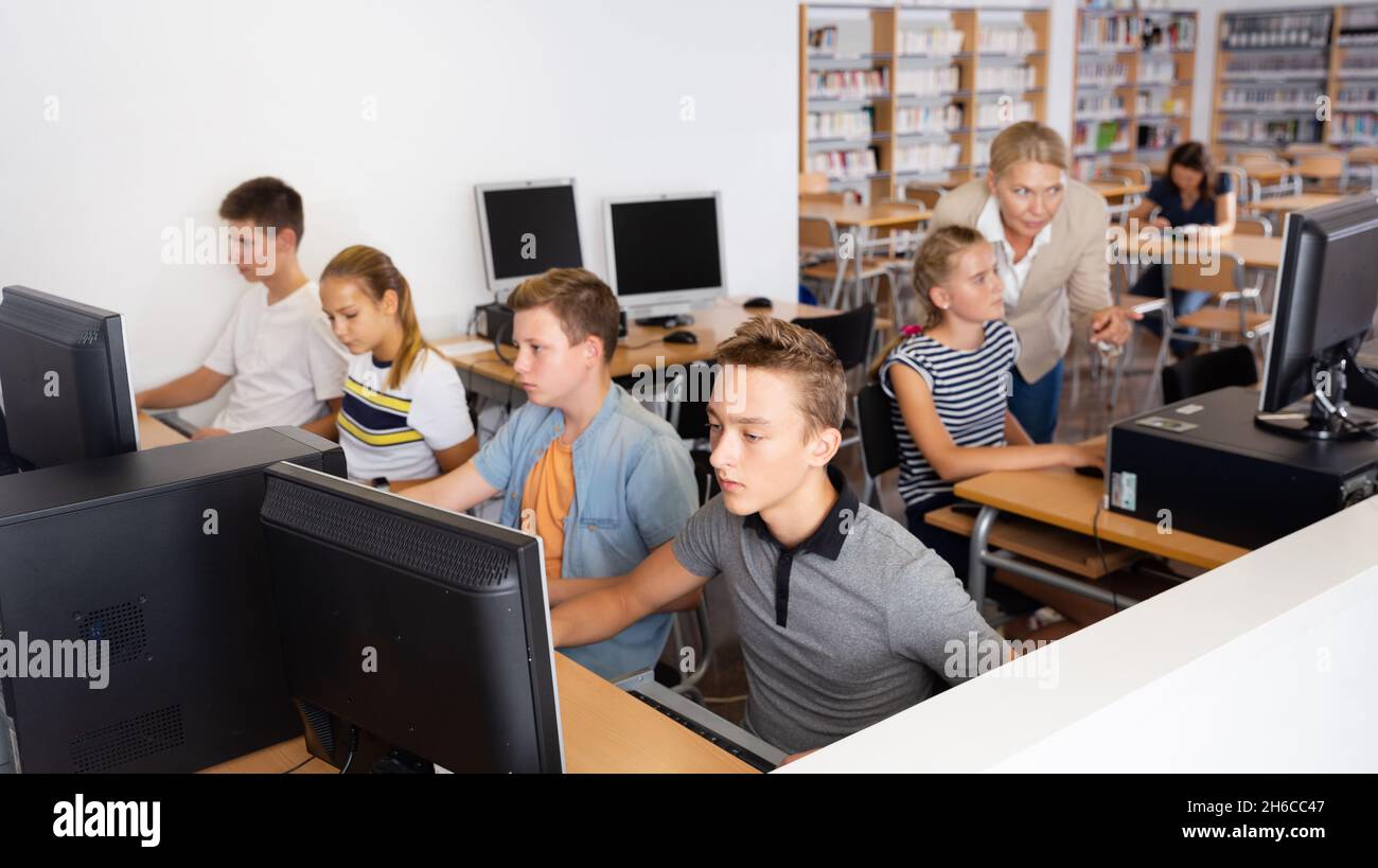 Schoolchildren using computers and teacher teaching them Stock Photo ...