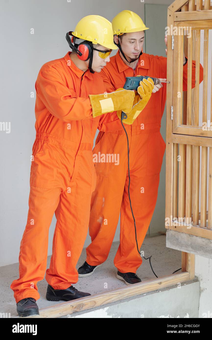 Two serious builders in uniform installing wooden frame and doors in ...