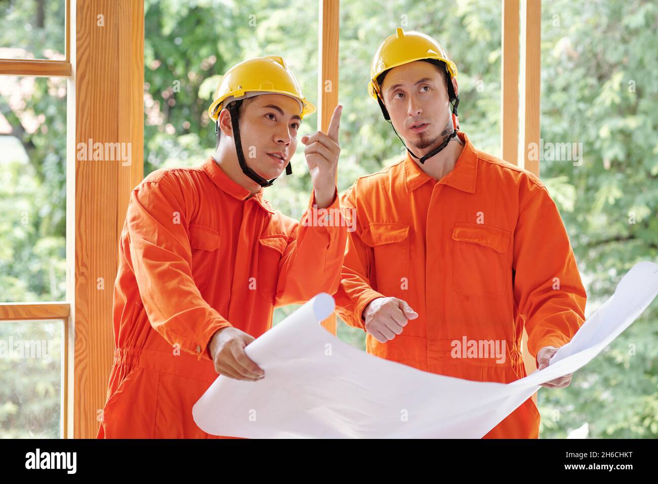 Builders with construction plan in hands discussing house walls they ...