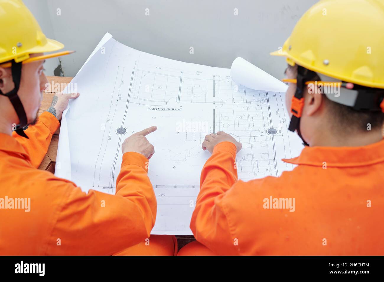 Builders in hardhats pointing at building blueprint, view from behind ...