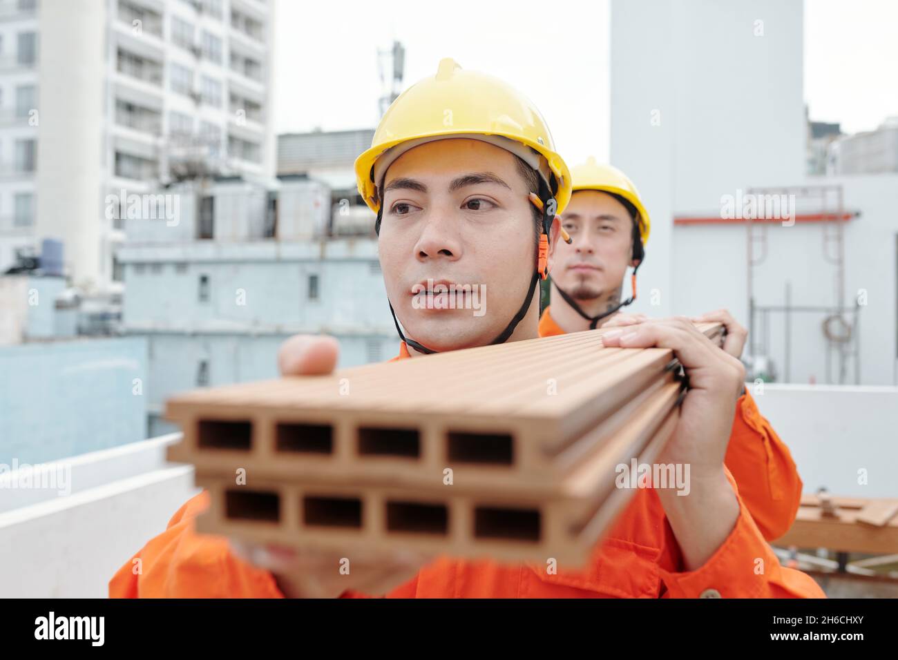 Construction site workers in hardhats carrying heavy wooden boards ...