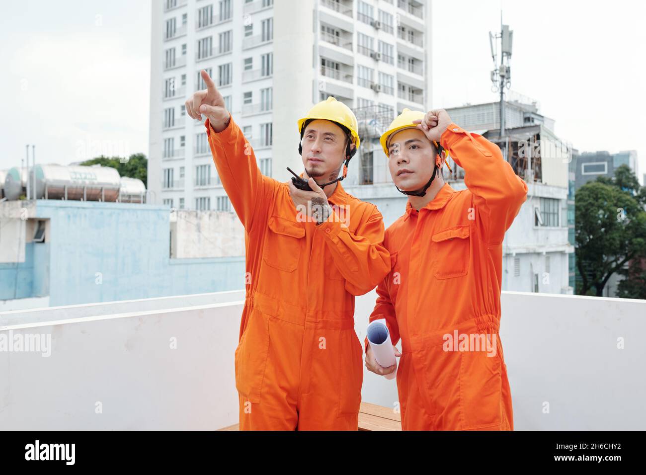 Team of construction site workers in hardhats talking on walkie-talkie ...