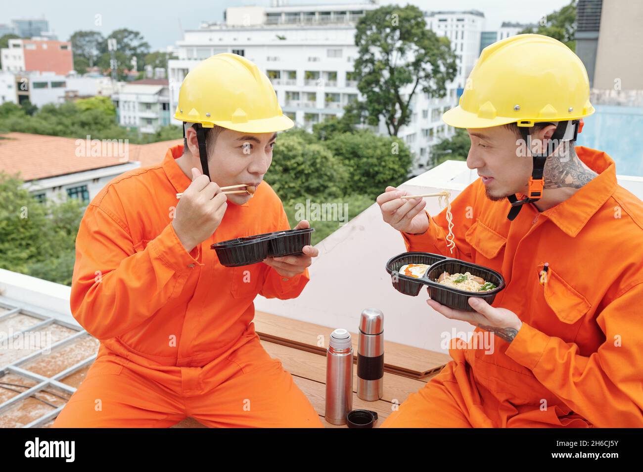 Construction workers sitting on building rooftop and eating ramen soup ...