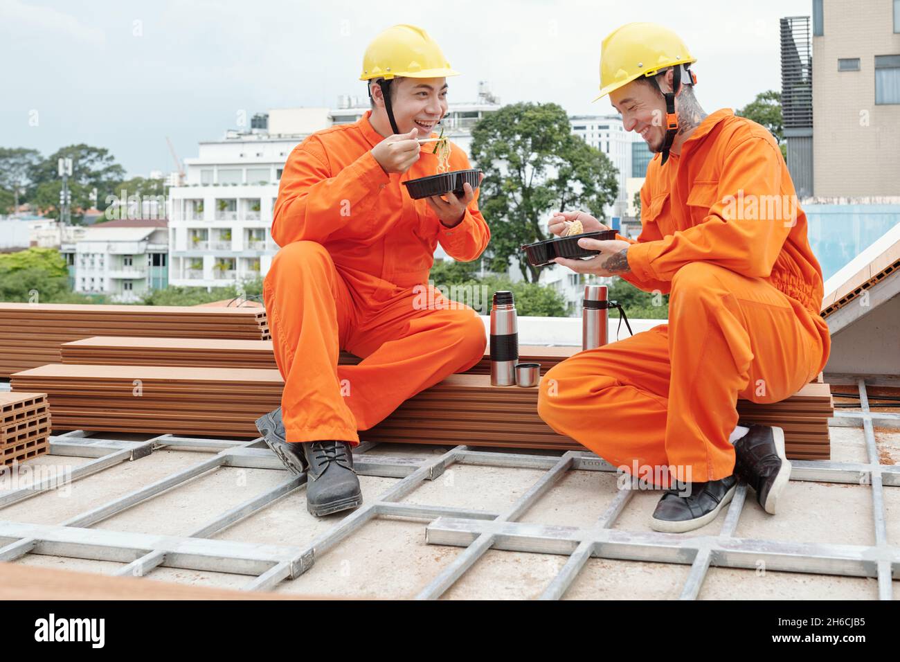Team of smiling builders eating lunch and drinking coffee on rooftop ...