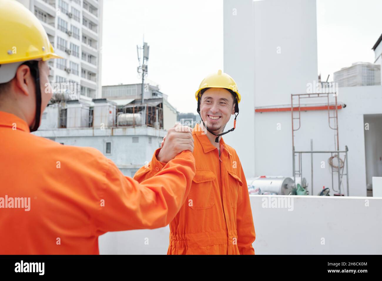 Cheerful construction worker shaking hand of his colleague after they ...