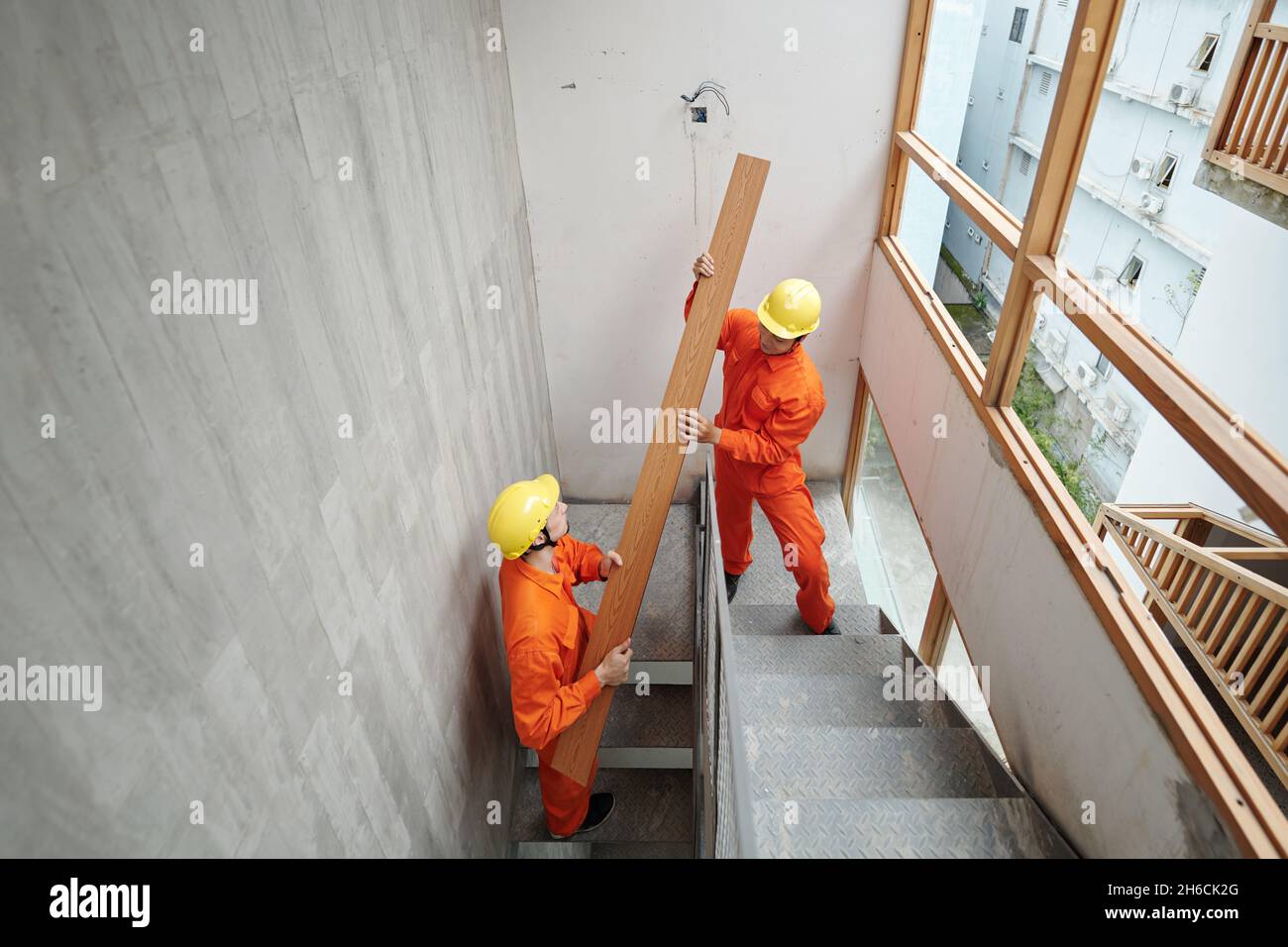 Workers carrying long board up the narrow stairs of house under ...