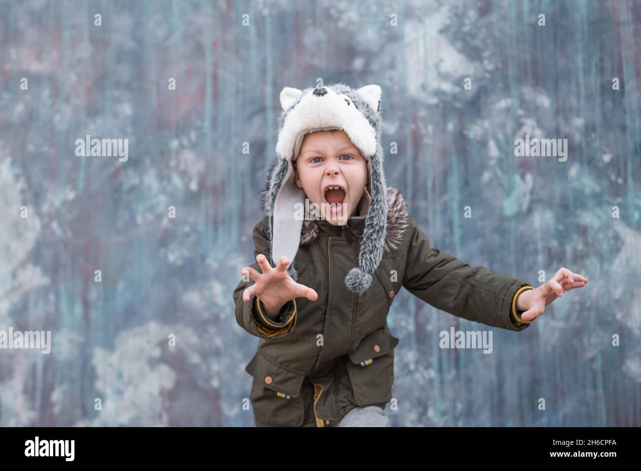 The roar of a wolf. Child in a wolf hat on gray background, outdoor ...
