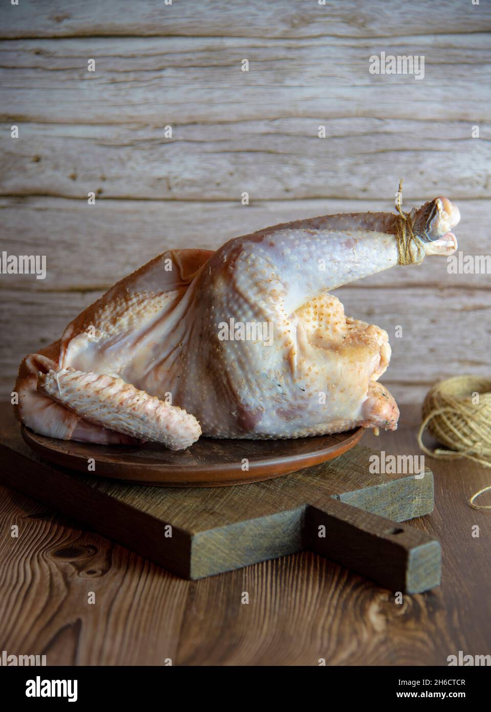 Fresh raw meat. A pale chicken carcass with its legs tied lies on a ...